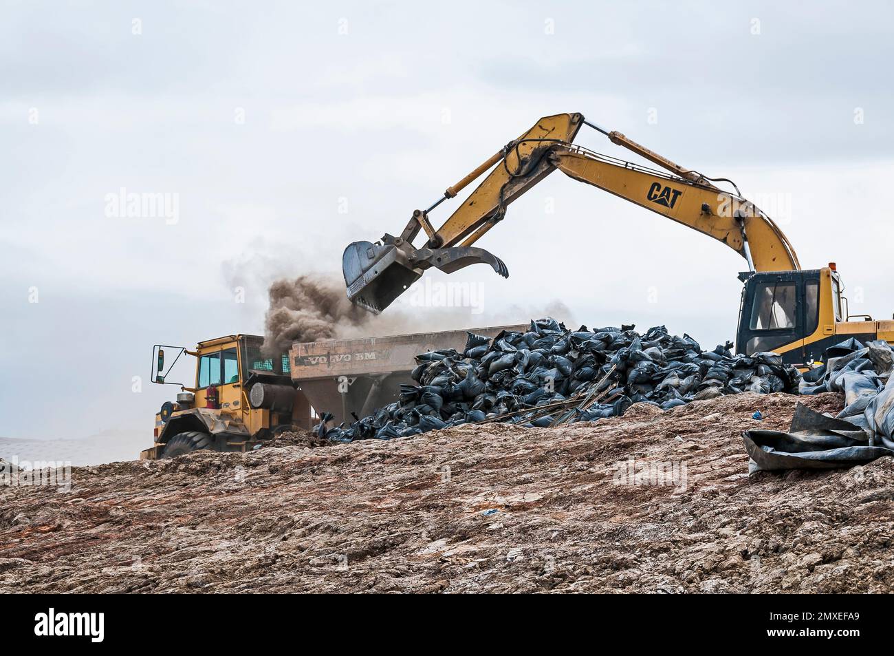 A power shovel loads solid waste into a large truck container for ...
