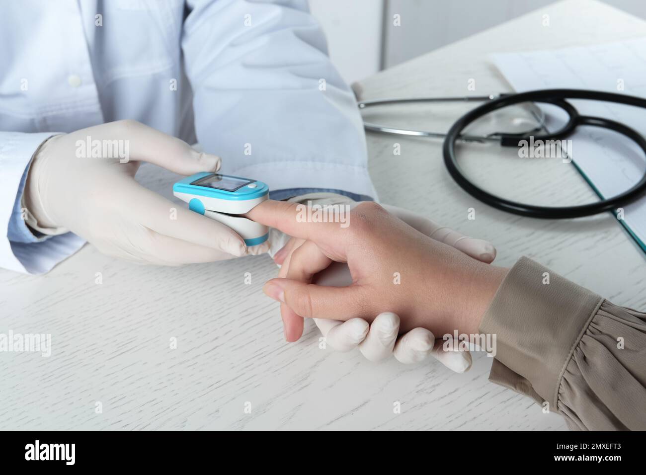 Doctor examining patient with fingertip pulse oximeter at white wooden ...