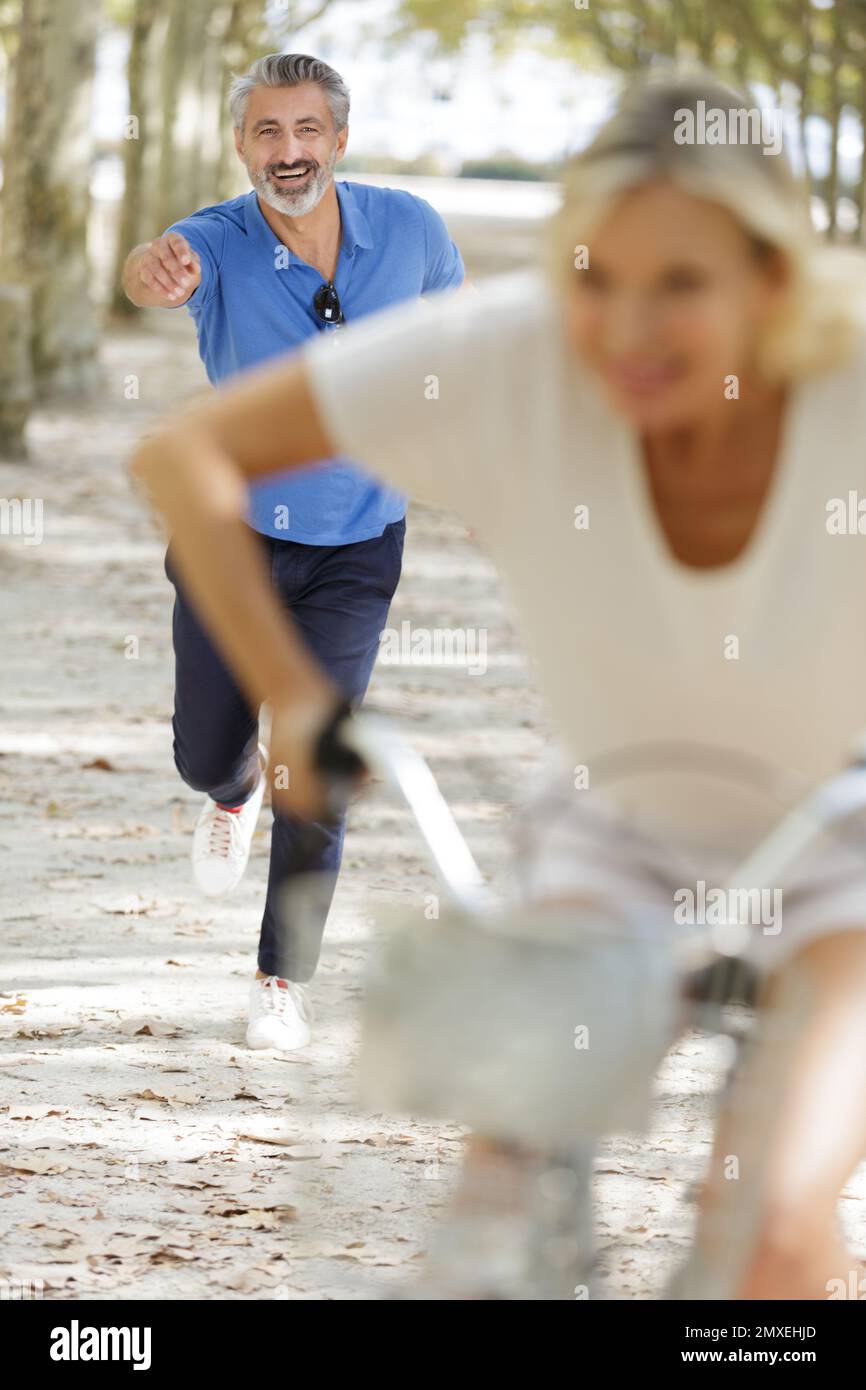 senior man playfully chasing woman on bicycle Stock Photo - Alamy