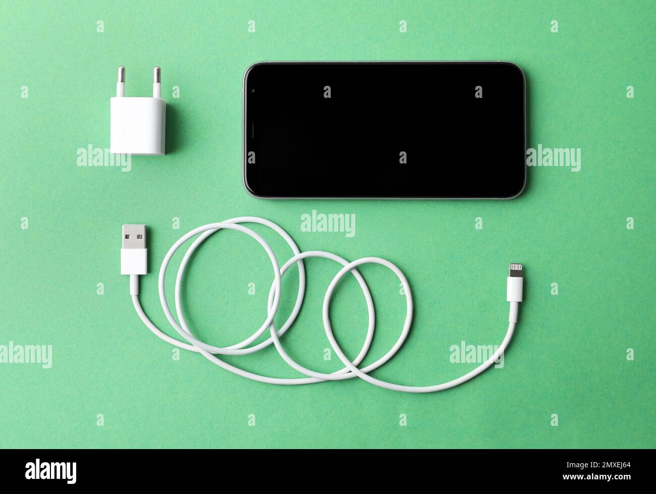 Smartphone and USB charger on green background, flat lay. Modern ...