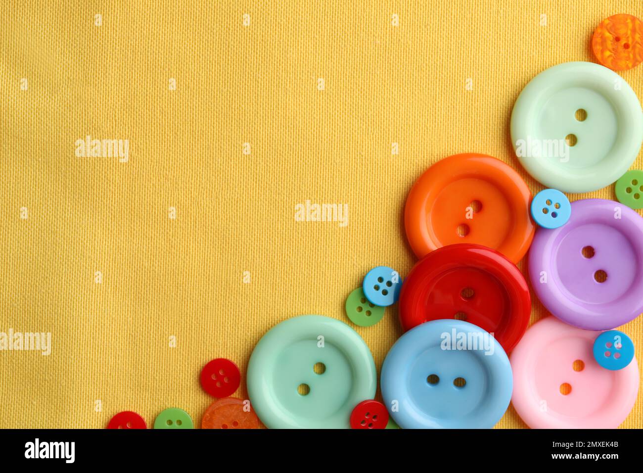Many bright sewing buttons on yellow fabric, flat lay. Space for text ...