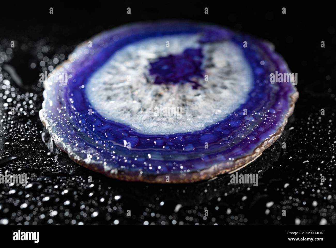 A close-up of a purple agate stone on a black background covered in ...
