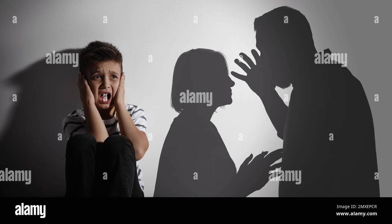 Scared little boy closing his ears and silhouettes of arguing parents ...