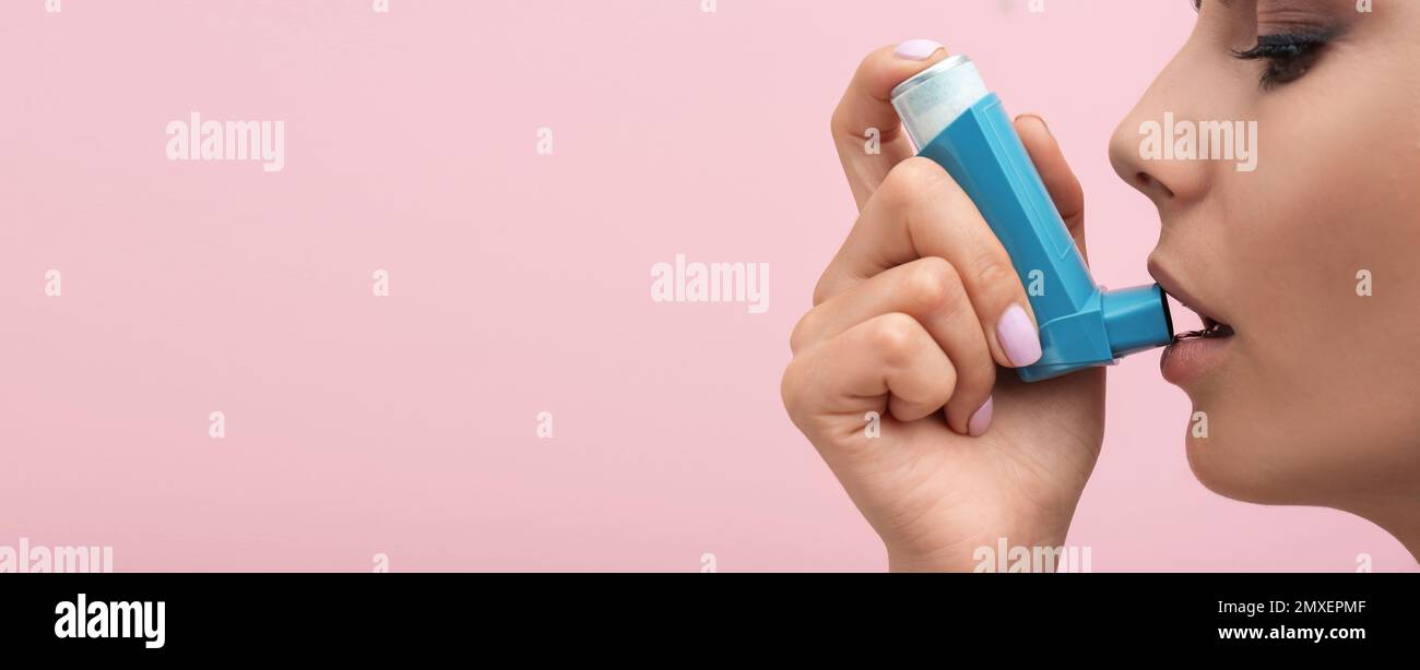 Young woman using asthma inhaler on pink background, space for text ...