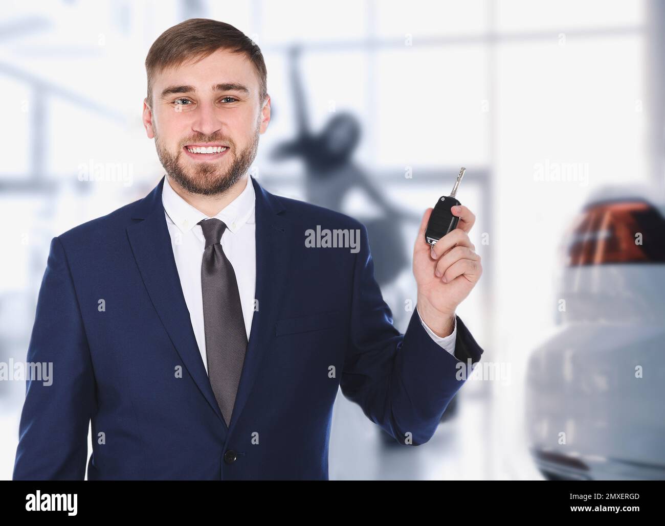 Happy salesman with key in car salon Stock Photo - Alamy
