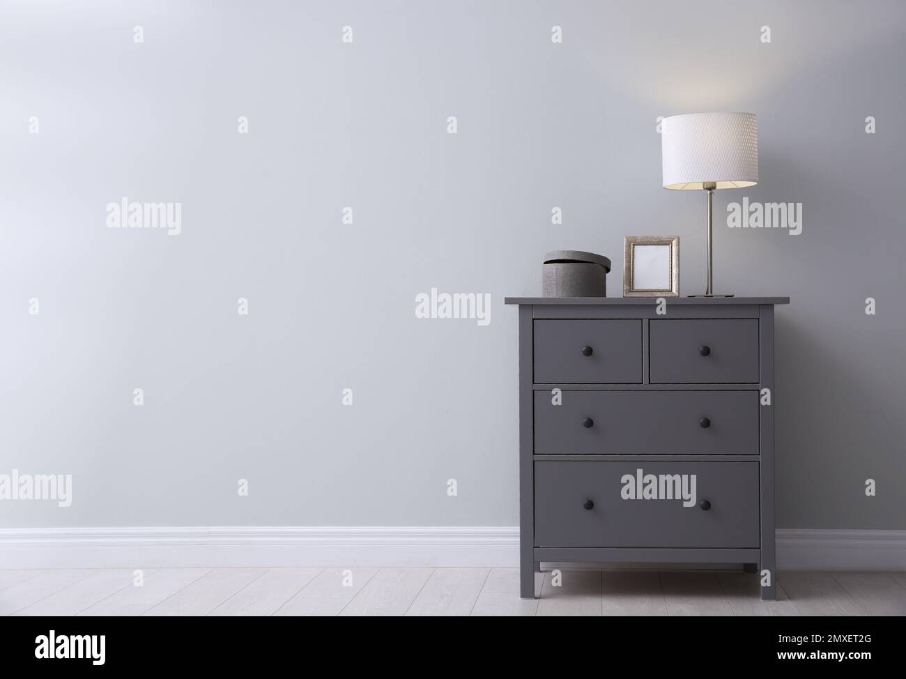 Modern grey chest of drawers near light wall in room, space for text ...