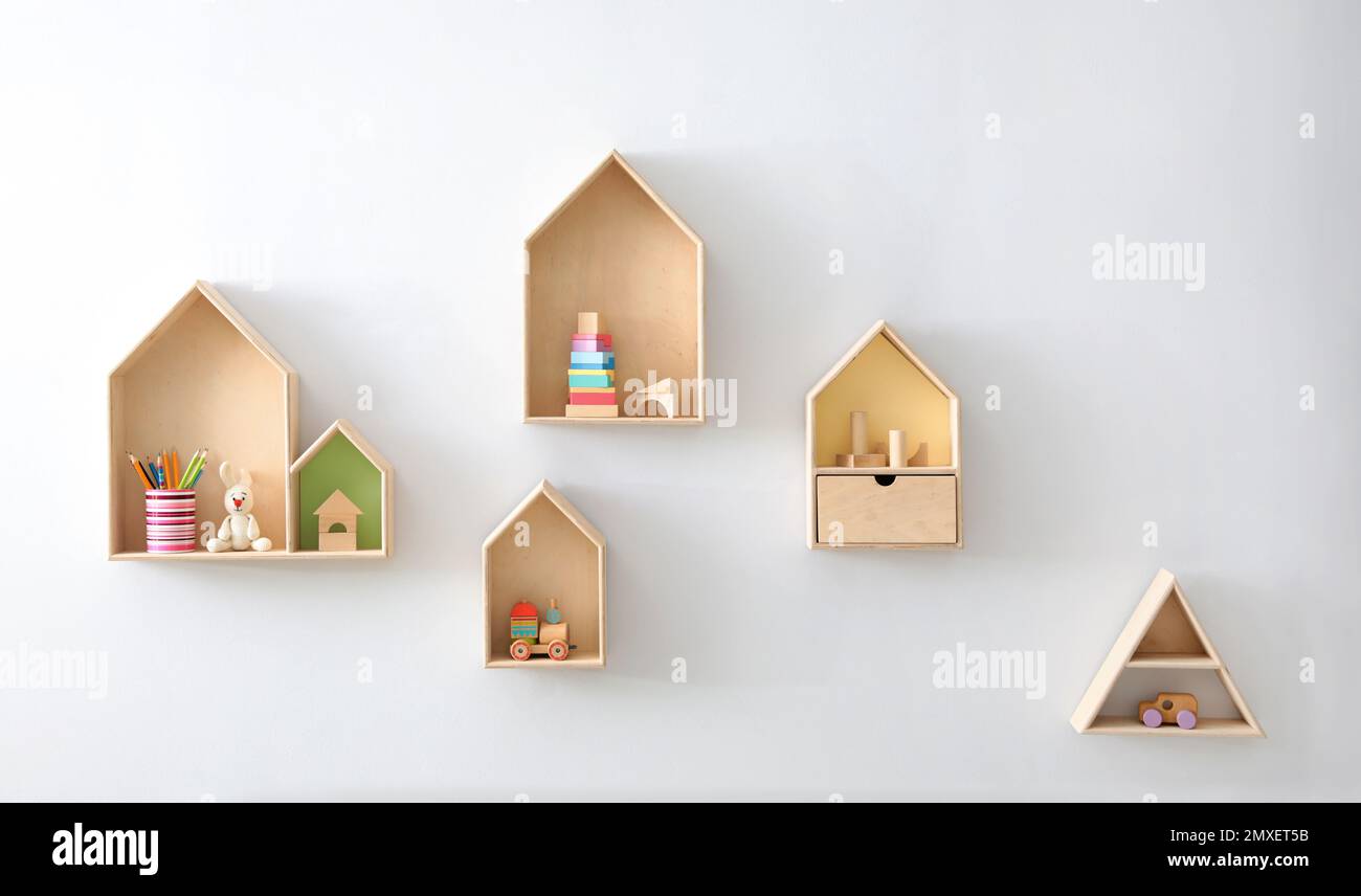 Different house shaped shelves with toys on white wall. Interior design ...