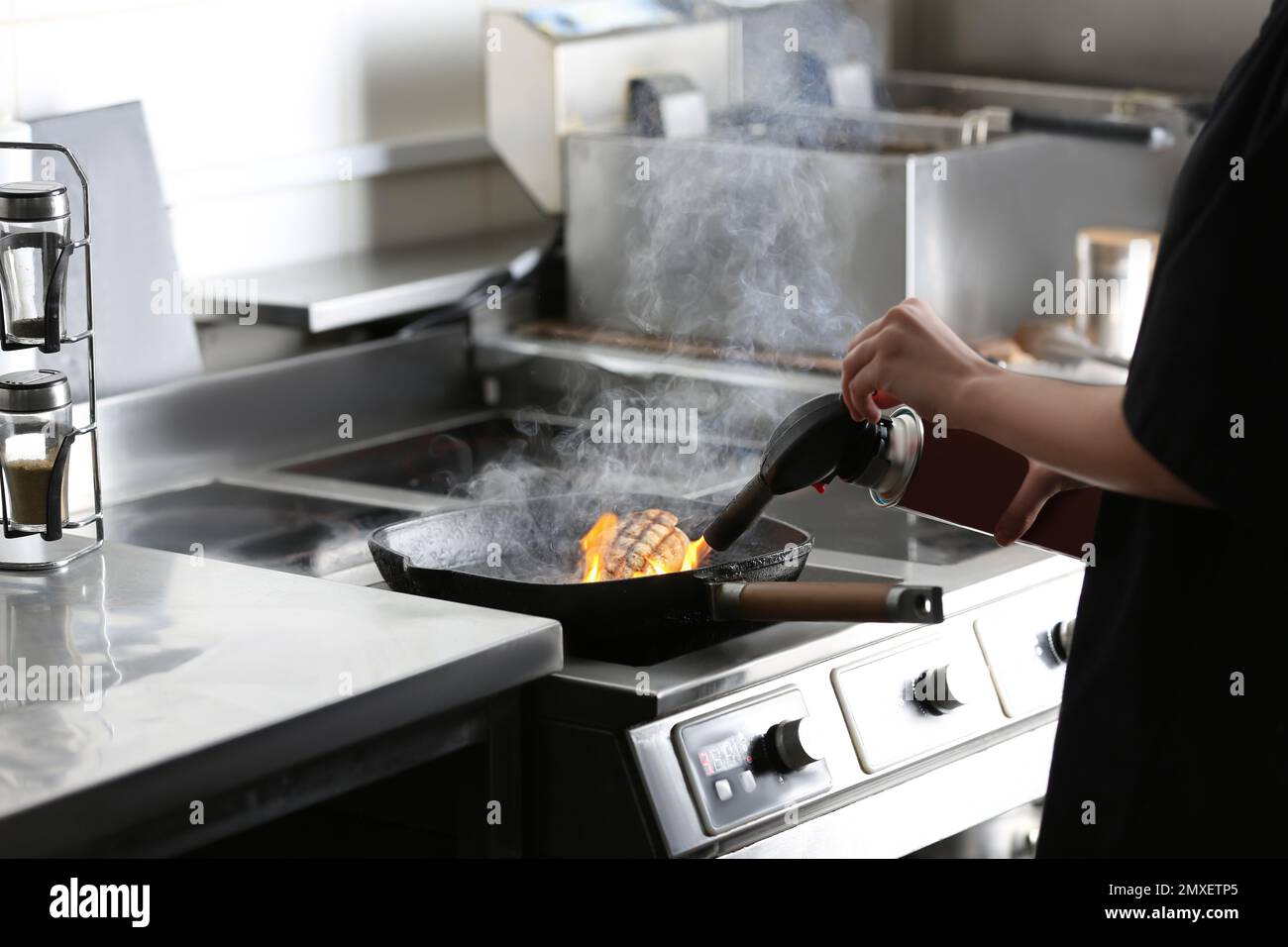 Female chef cooking meat with manual gas burner on stove in restaurant ...
