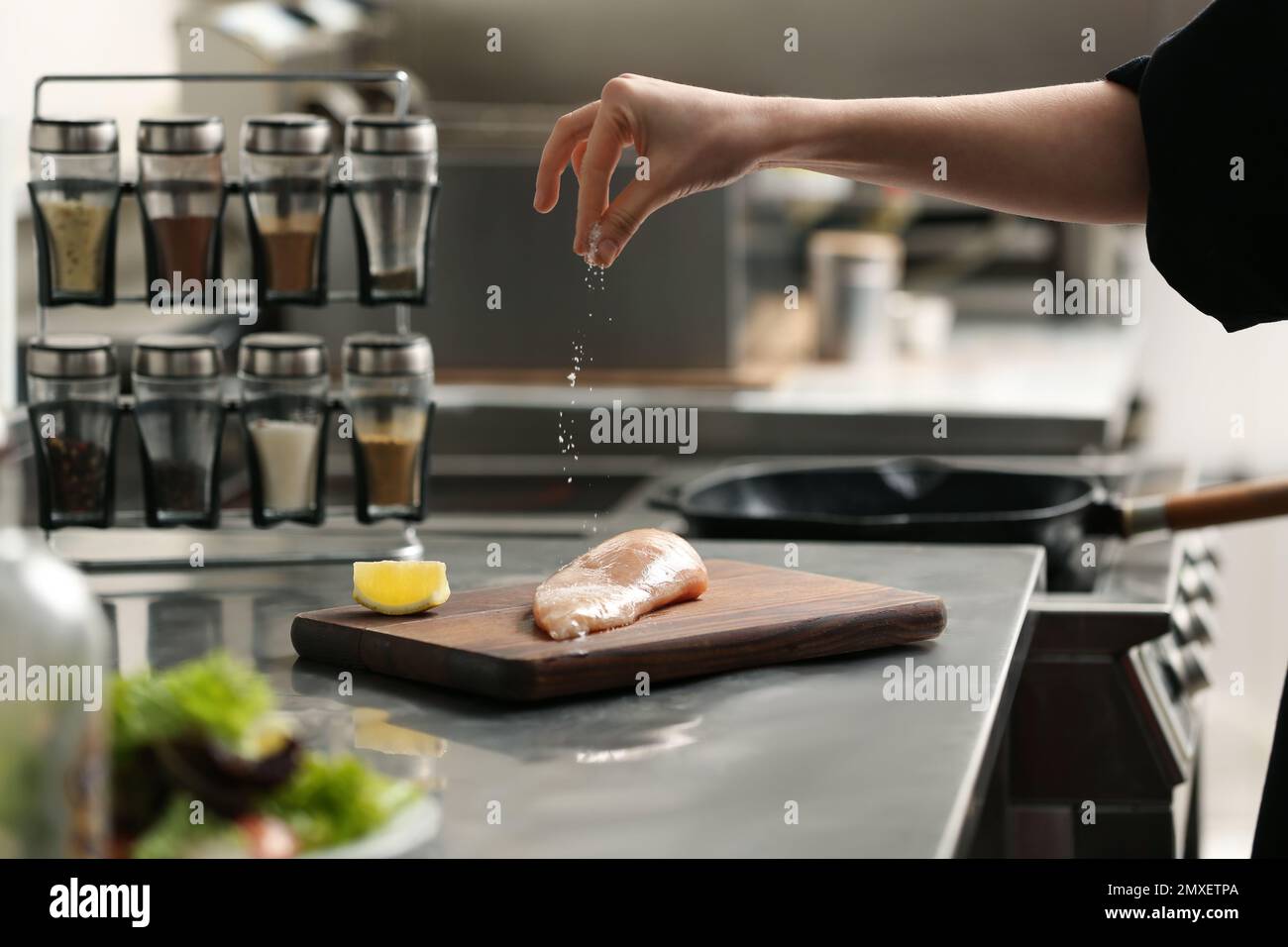 Female chef adding salt to raw chicken fillet in restaurant kitchen ...
