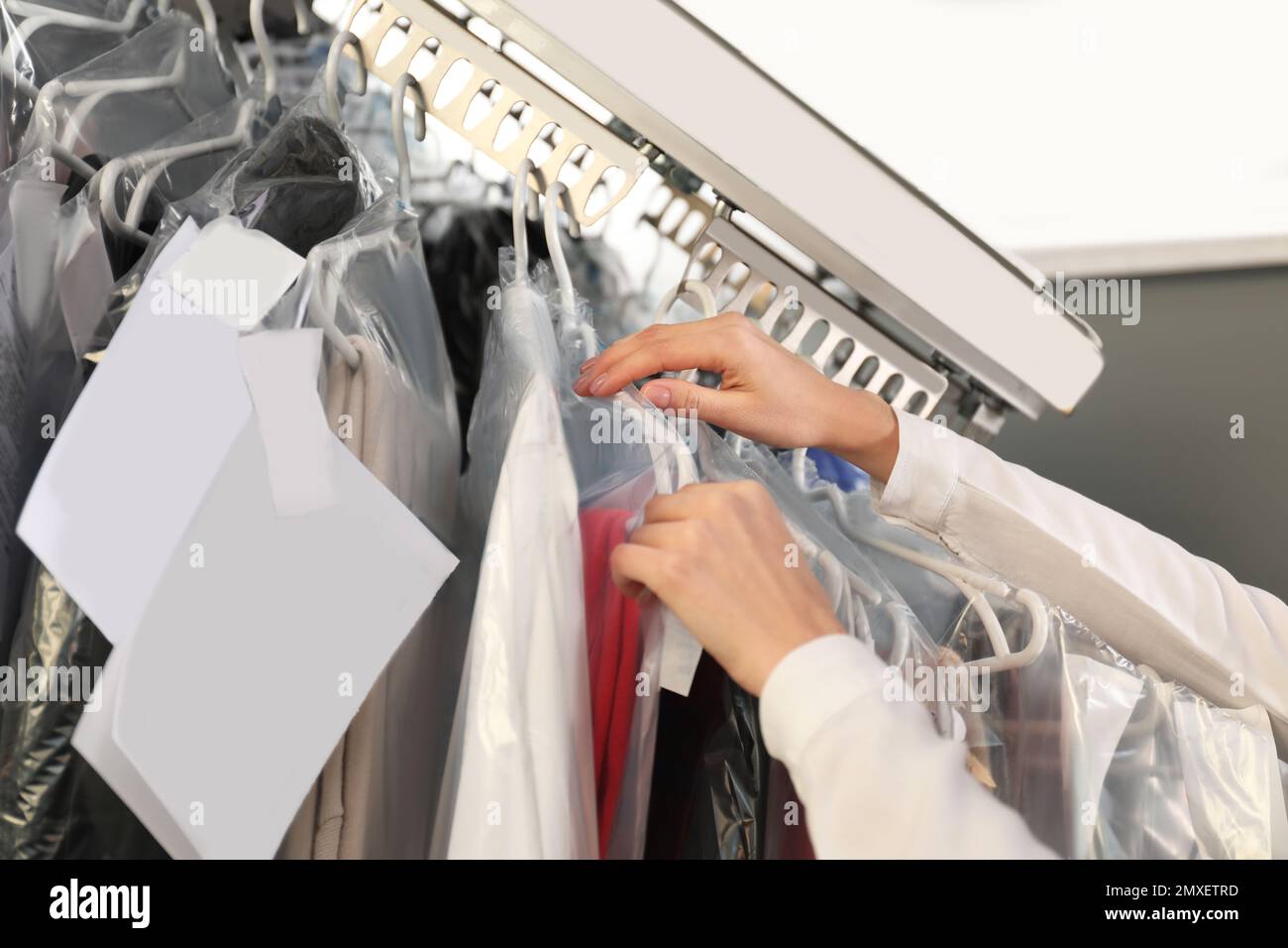 Female worker taking clothes from garment conveyor at dry-cleaner's ...