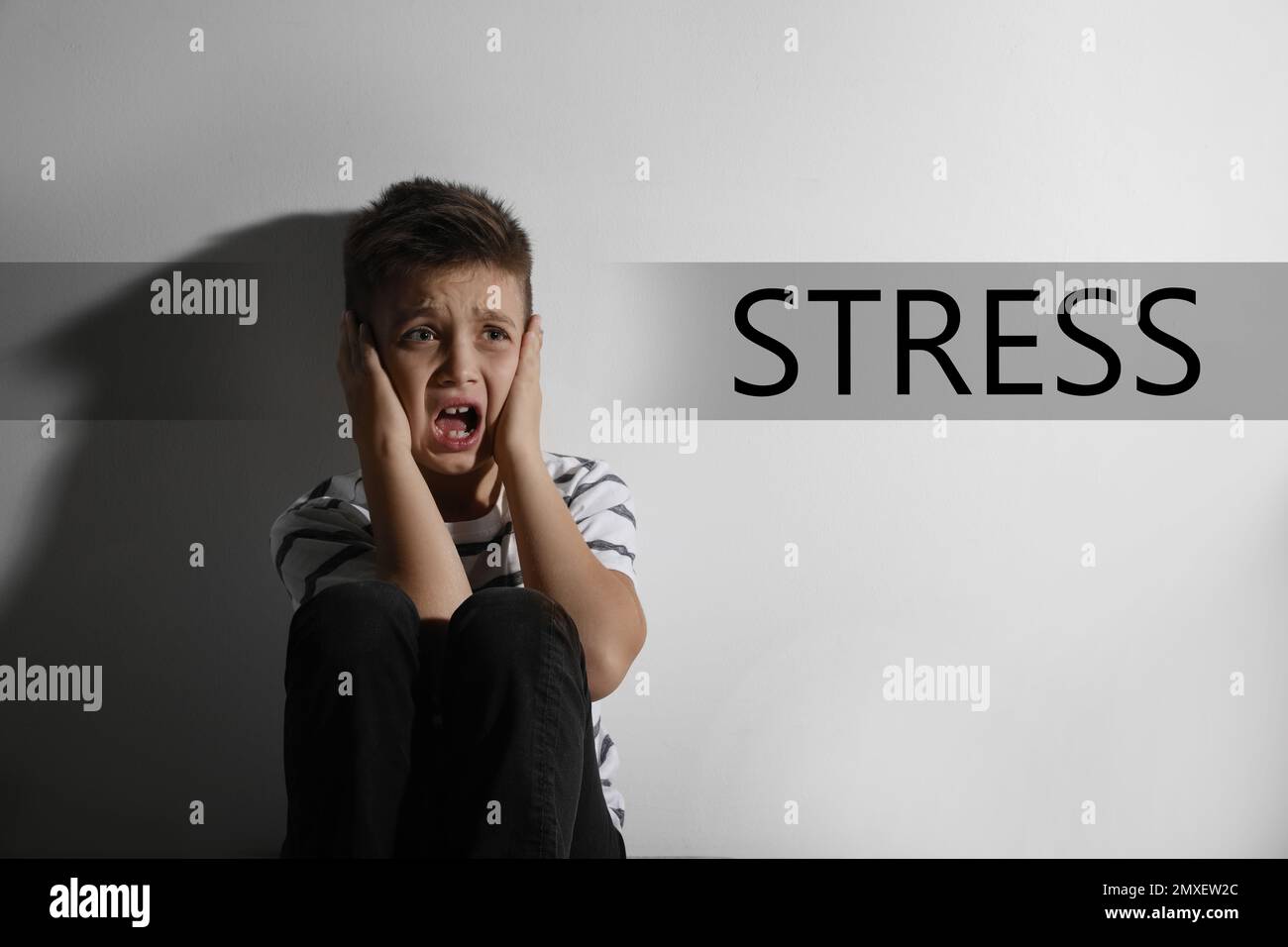 Scared little boy near white wall and word STRESS Stock Photo - Alamy