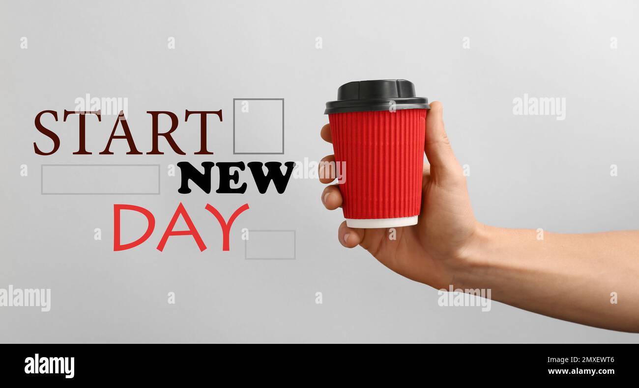 Man holding paper coffee cup and phrase START NEW DAY on light ...