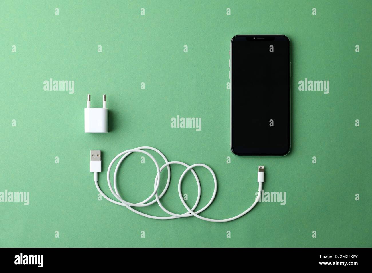 Smartphone and USB charger on green background, flat lay. Modern ...