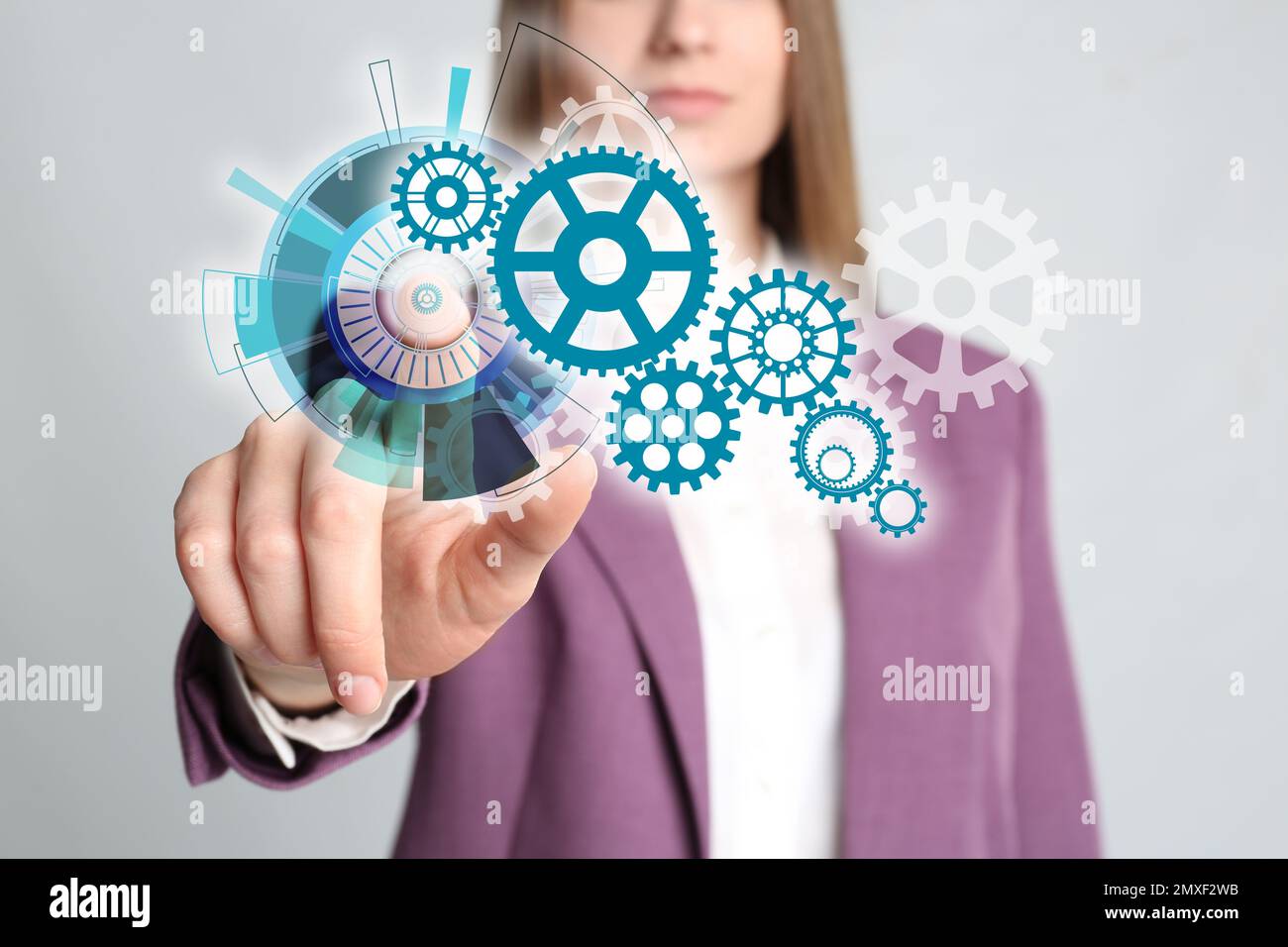 Young woman touching gear mechanism on light grey background, closeup ...