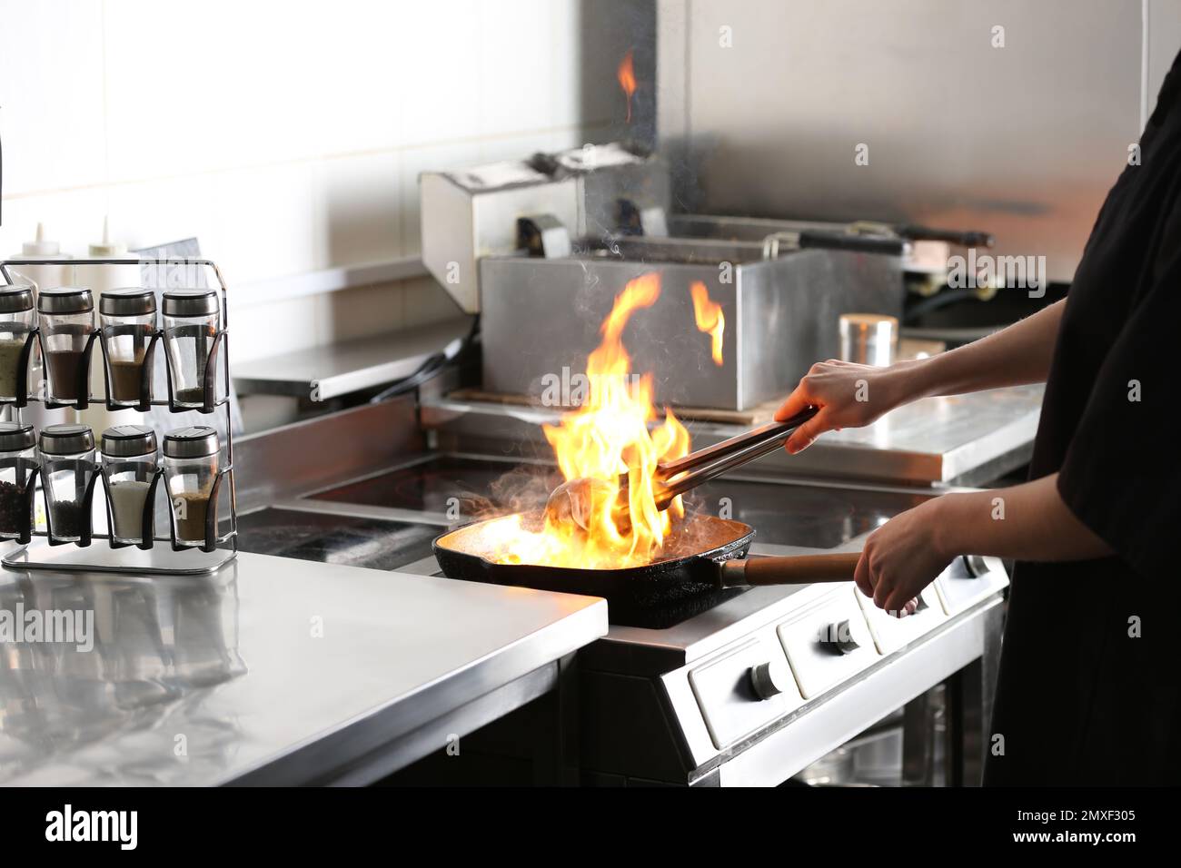 Female chef cooking meat with burning flame on stove in restaurant ...