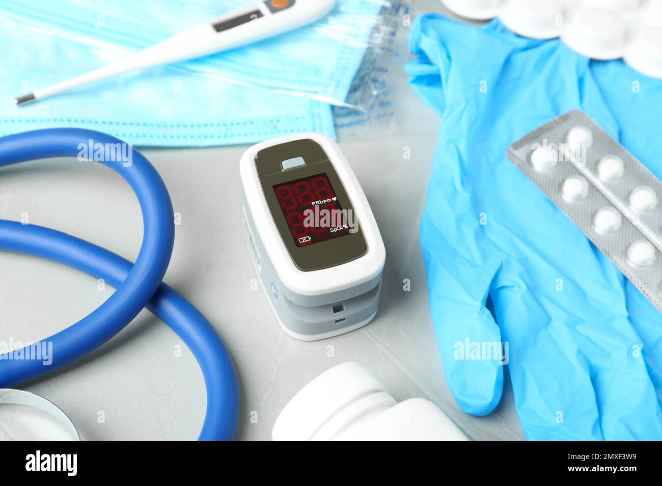 Modern fingertip pulse oximeter and medical items on light grey stone ...