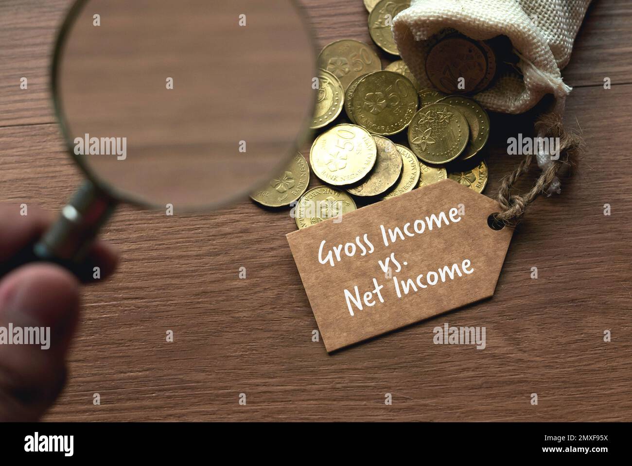 A hand holding a magnifying glass pointing to a bag of gold coins with ...