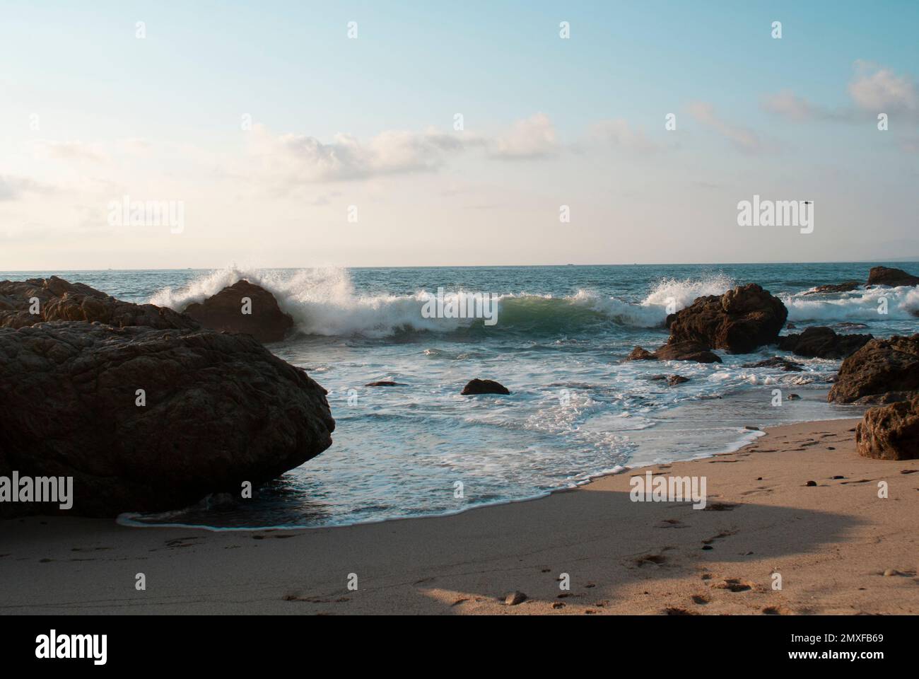A seascape view with water waves hitting on rocky cliffs, sunlit sky ...