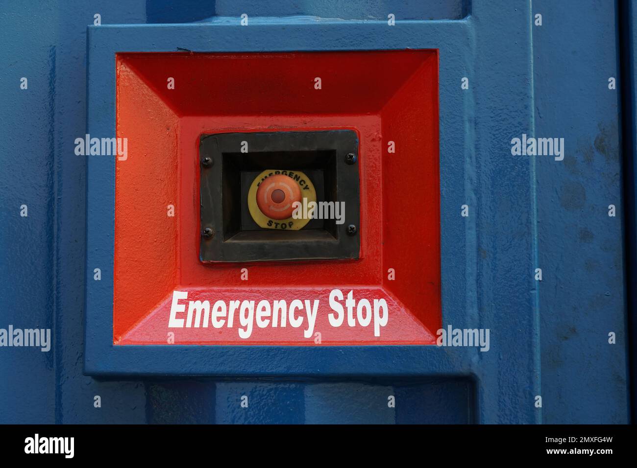 Red Emergency stop button placed on the wall of blue container of ...