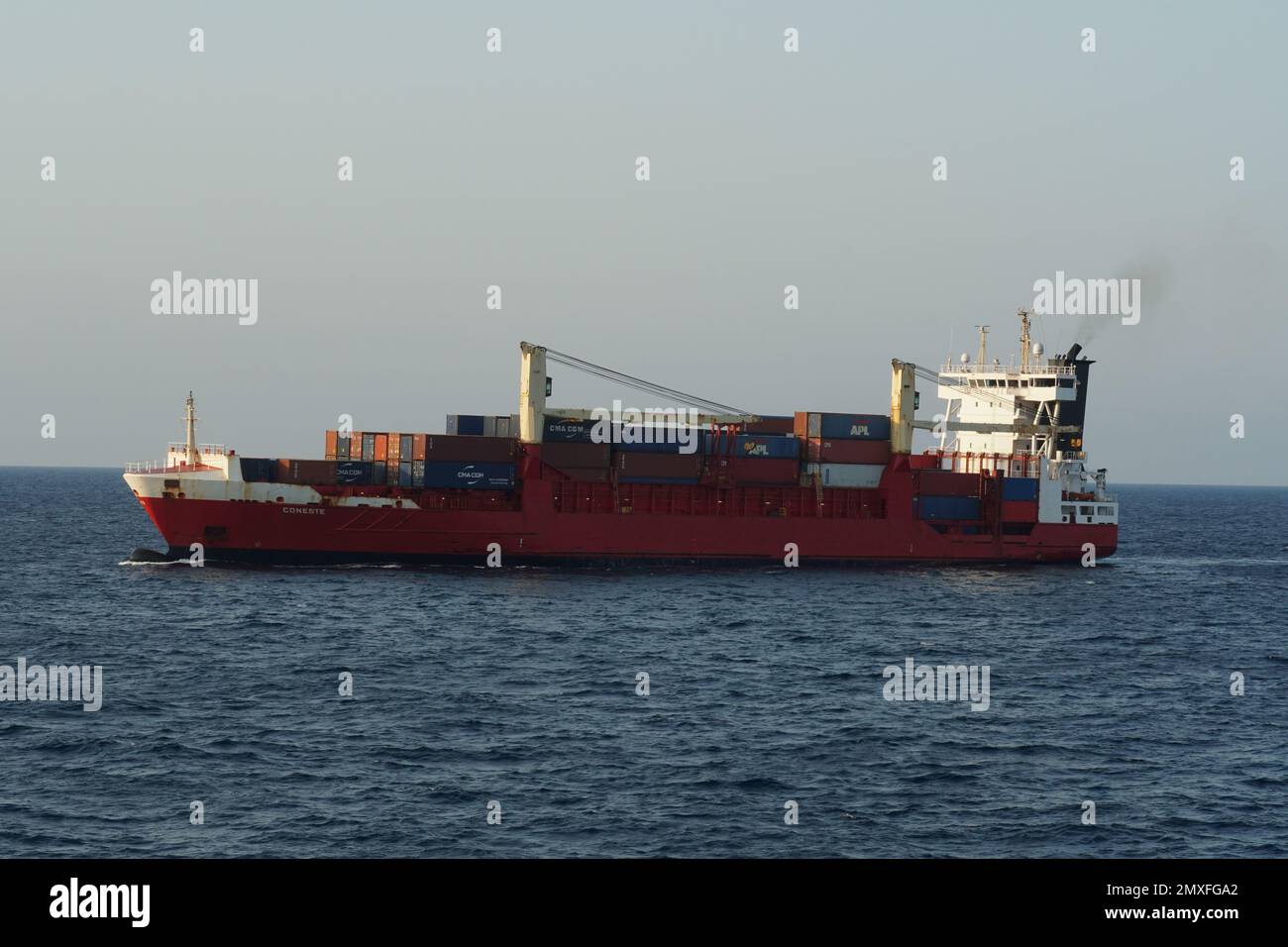 Loaded container vessel with red hull and equipped with two cargo ...