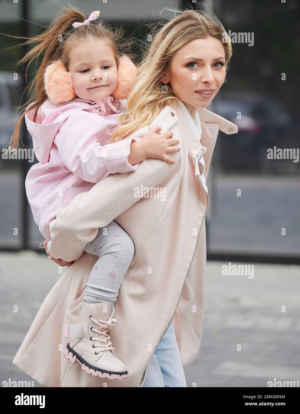 Blonde woman with little girl on her back standing on the street ...