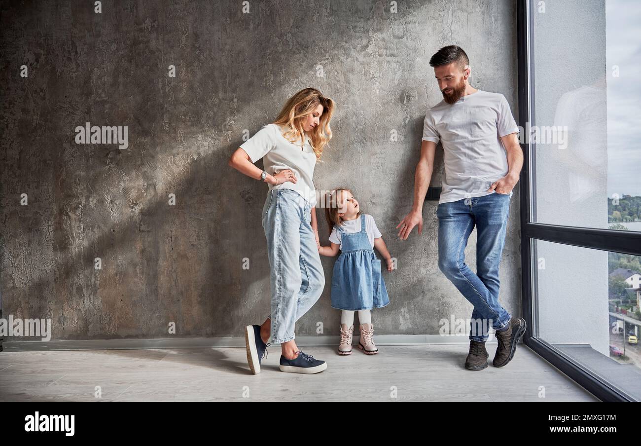 Happy parents and child standing by the window against the wall in ...