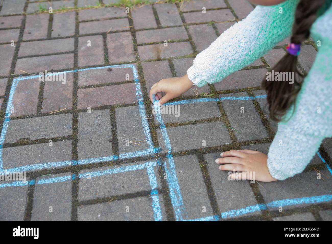 girl draws a hopscotch with chalk on the pavement.Child playing the ...
