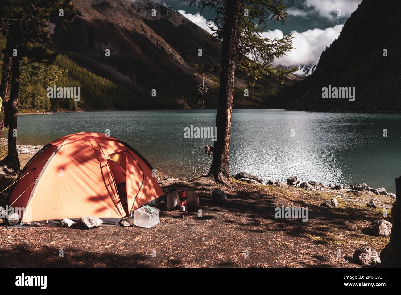 An orange tent stands in the trees on the shore of the high-altitude ...