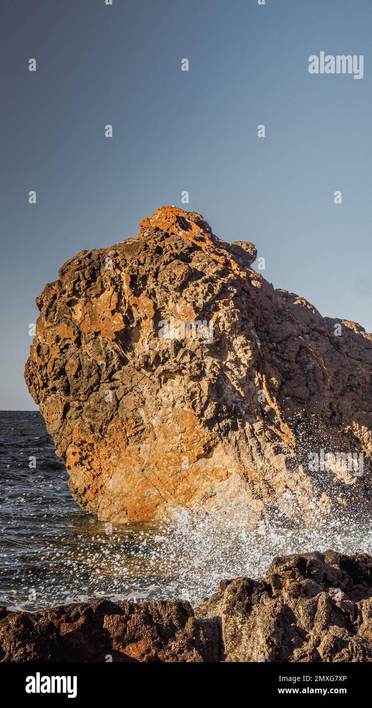 A massive rock sticking out towards the sea at a coast against a clear ...