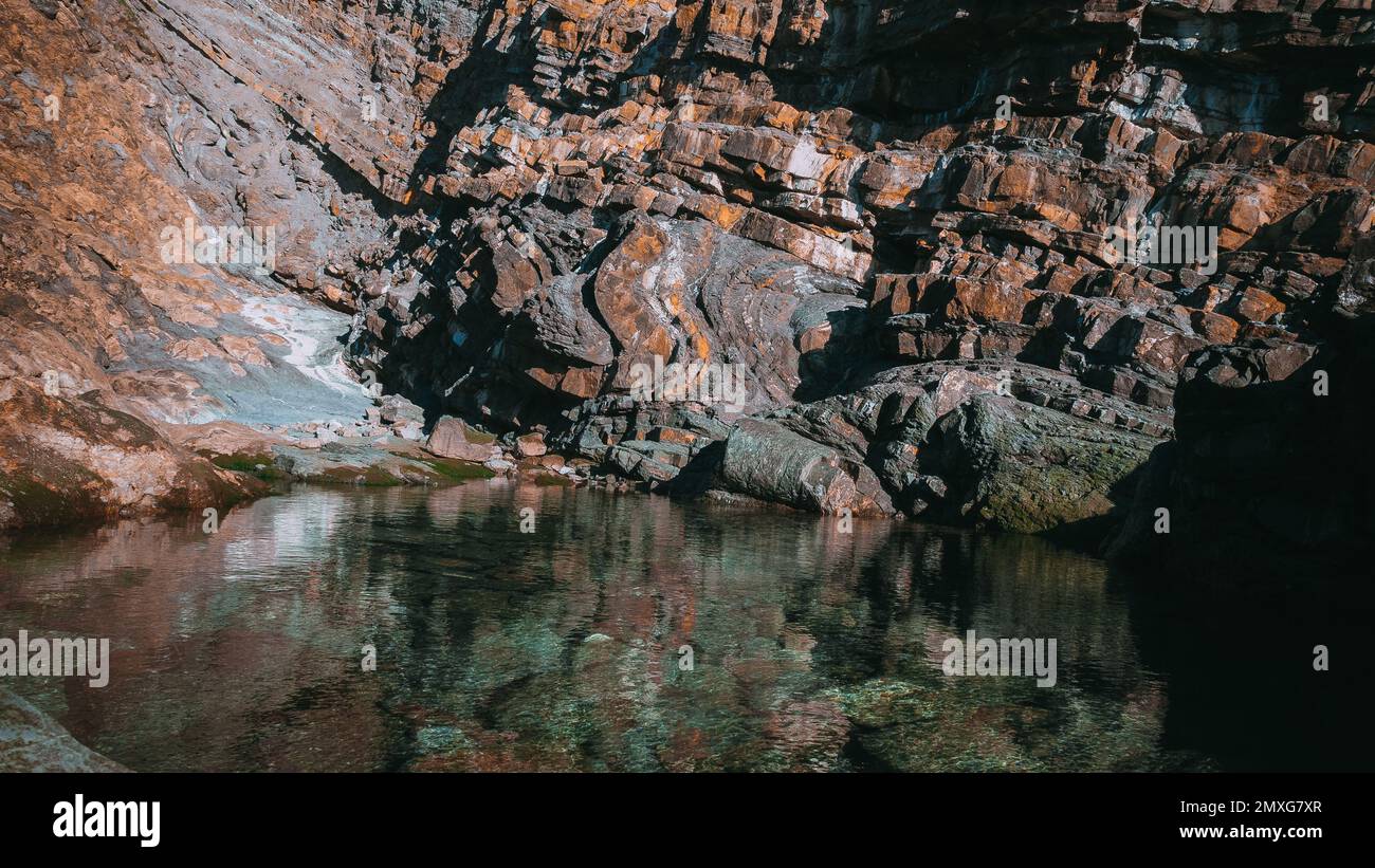 A fresh, clean water source beside a colorful rock wall Stock Photo - Alamy