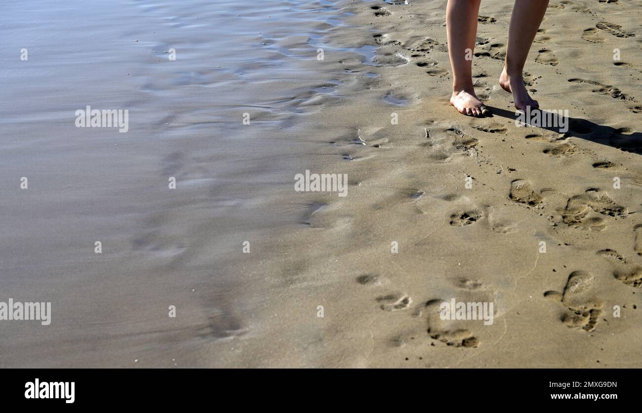 Legs and feet of barefoot person walking along sandy beach at waters ...