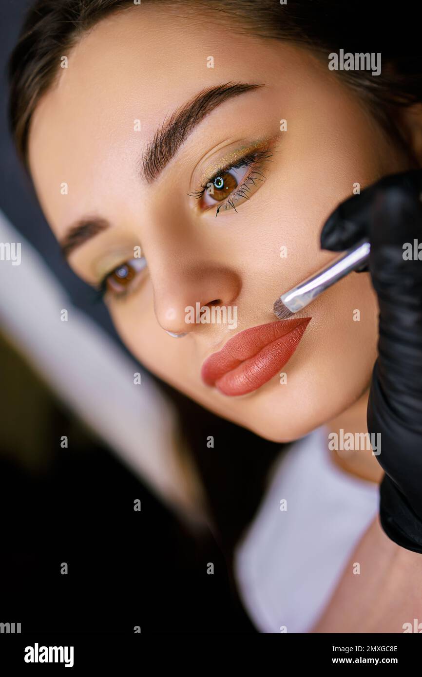 Applying foundation with a brush around the lip contour after permanent ...