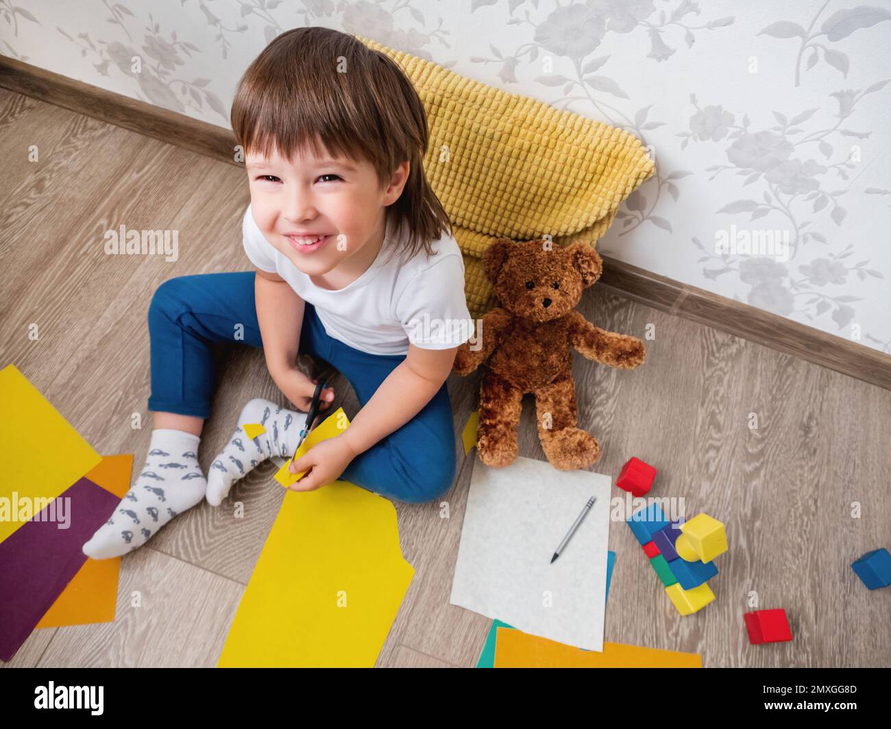 Toddler boy learns to cut colored paper with scissors. Kid sits on ...