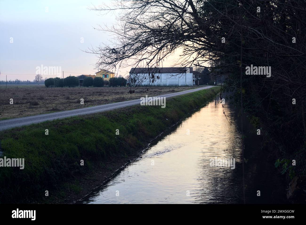 Stream of water and road next to a field at sunset in the italian ...