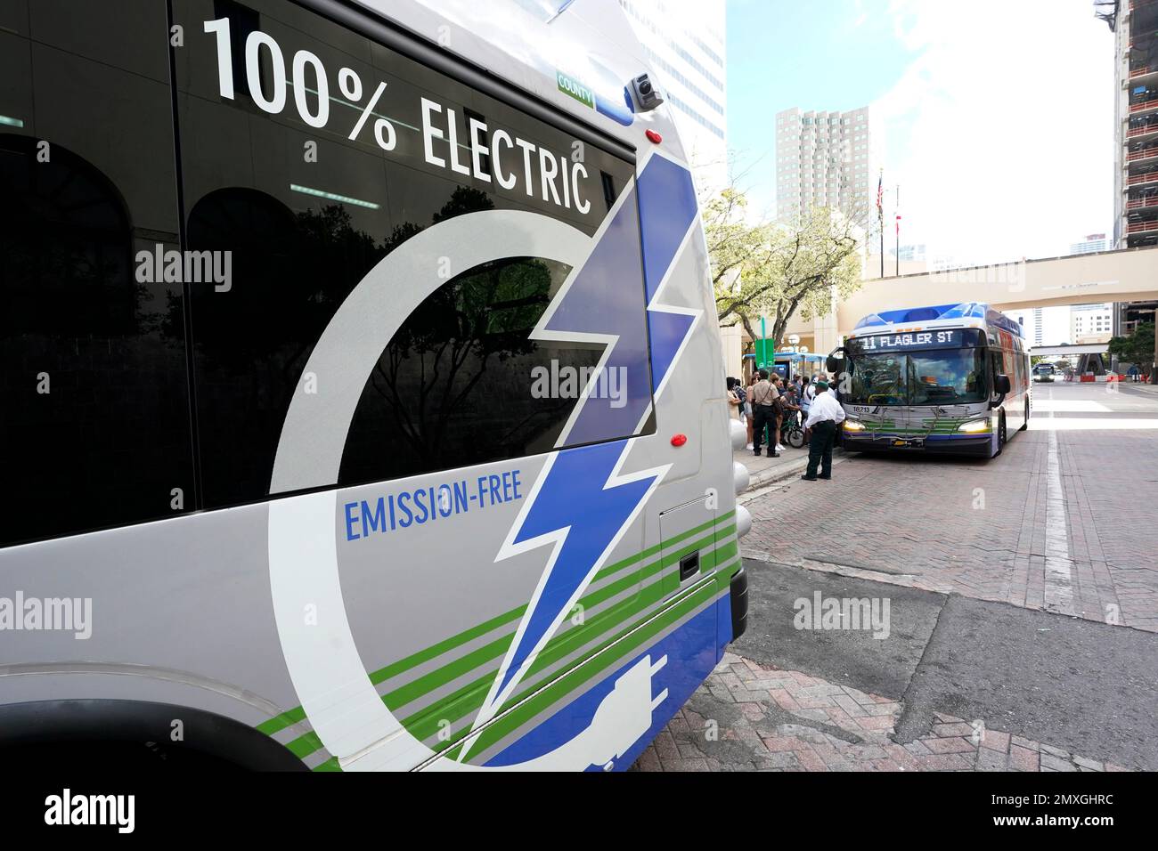 A new battery-powered bus, left, is shown parked at a bus stop ...