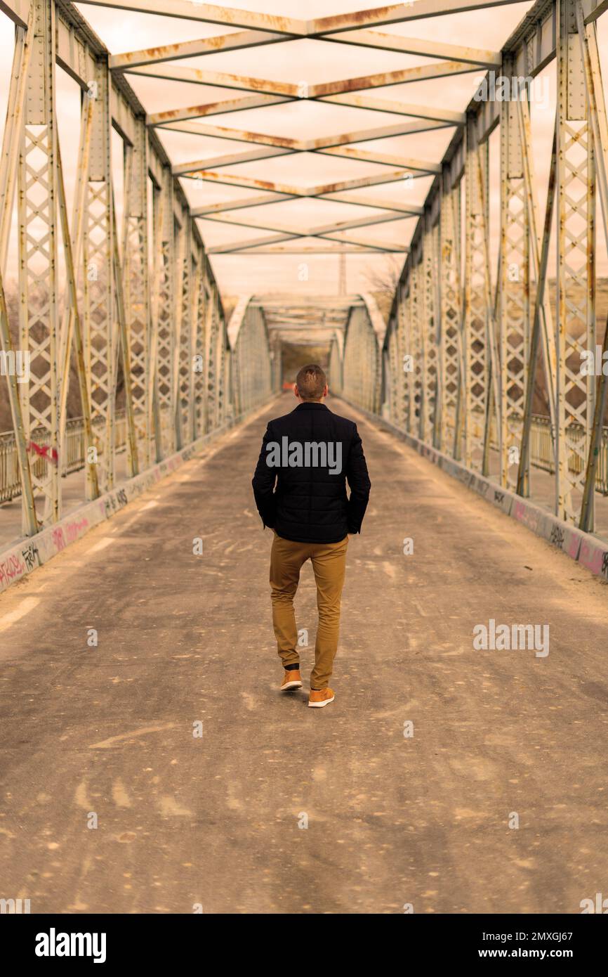 A vertical shot of a back of a man walking on a bridge Stock Photo - Alamy