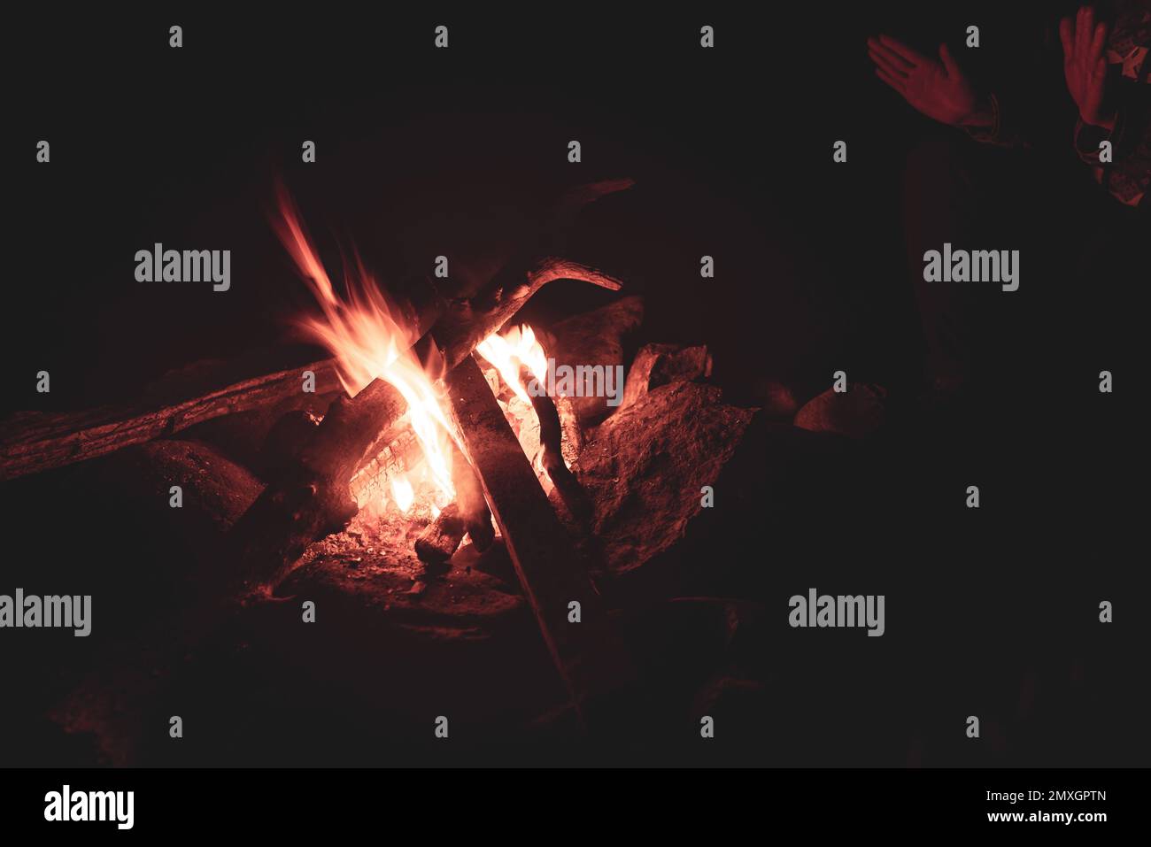 The girl warms the palms of her hands near the warm flame of a fire ...