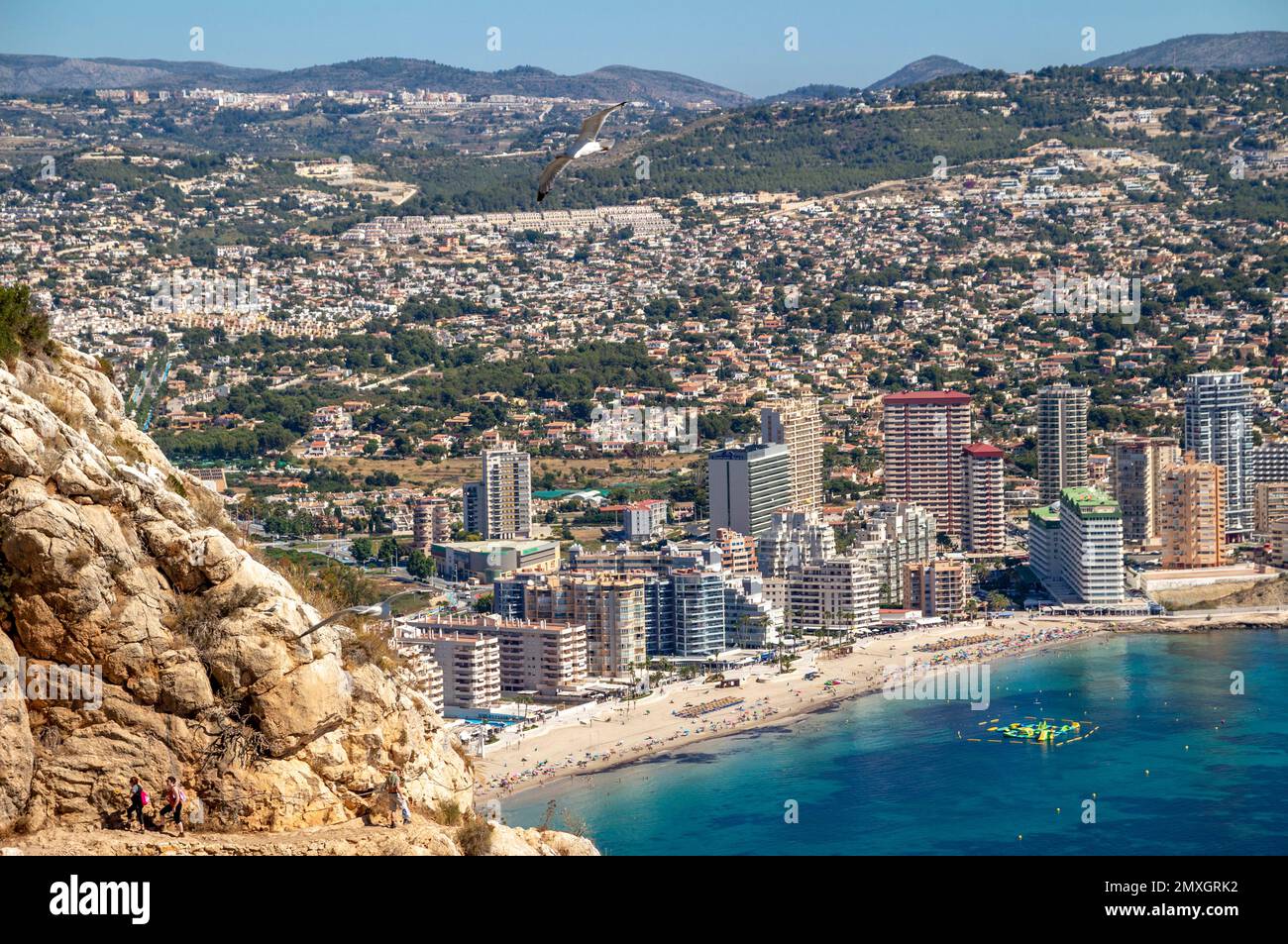 beach with buildings and seagulls flying and people hiking. Rock of ...