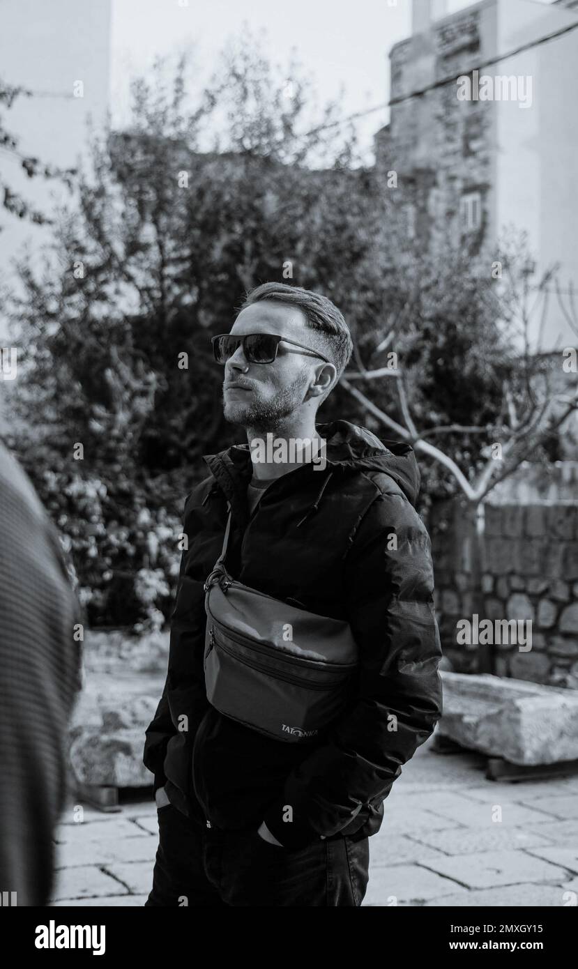 A vertical grayscale shot of a guy with glasses in a jacket looking ...