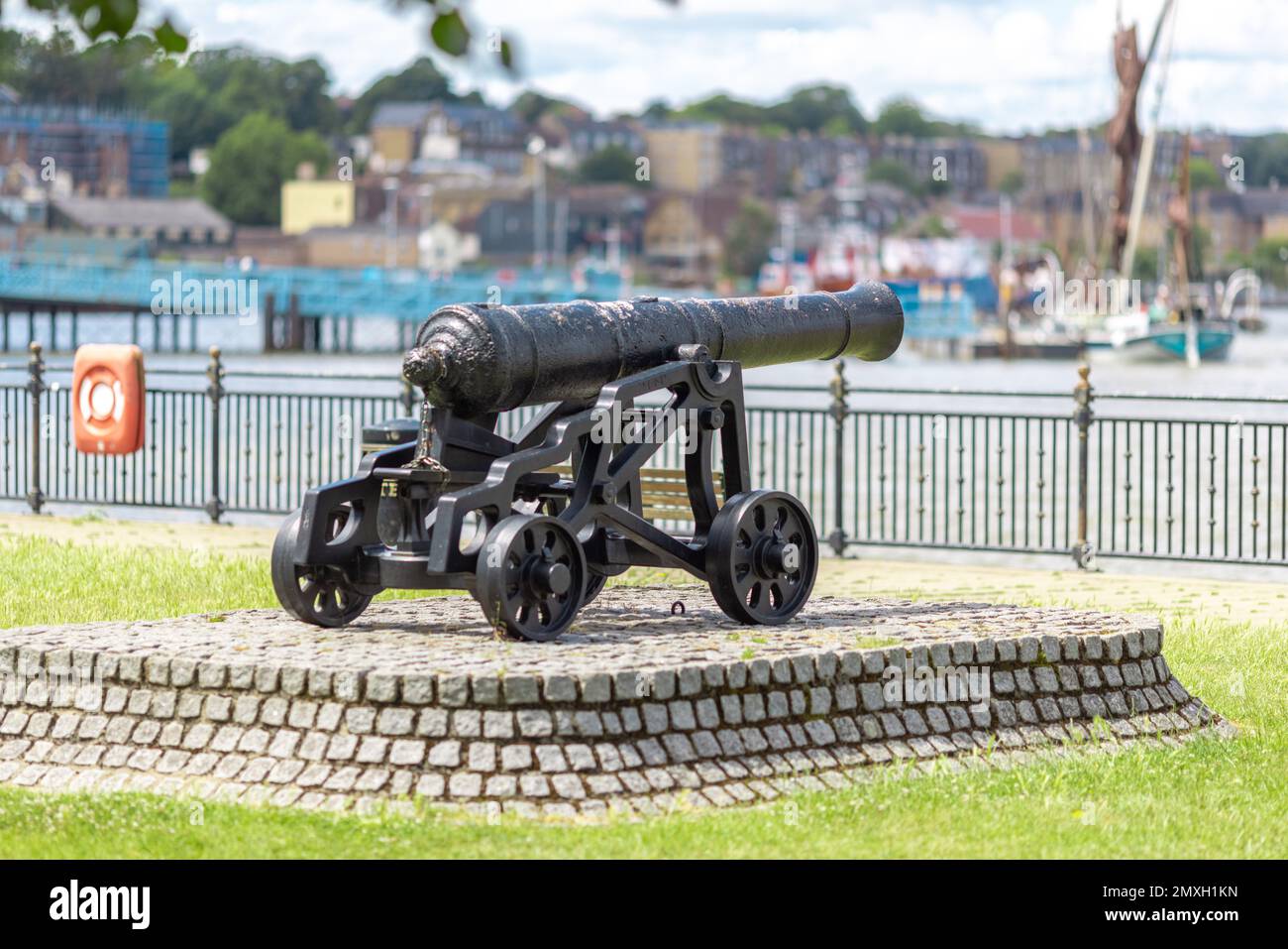 An old cannon on display at a park witn city buildings in the ...