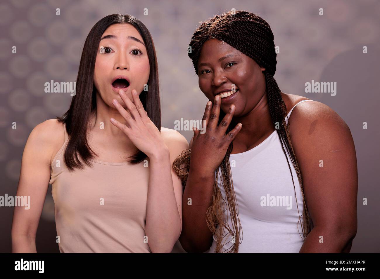 Two diverse surprised women laughing with hand over mouth, hearing ...