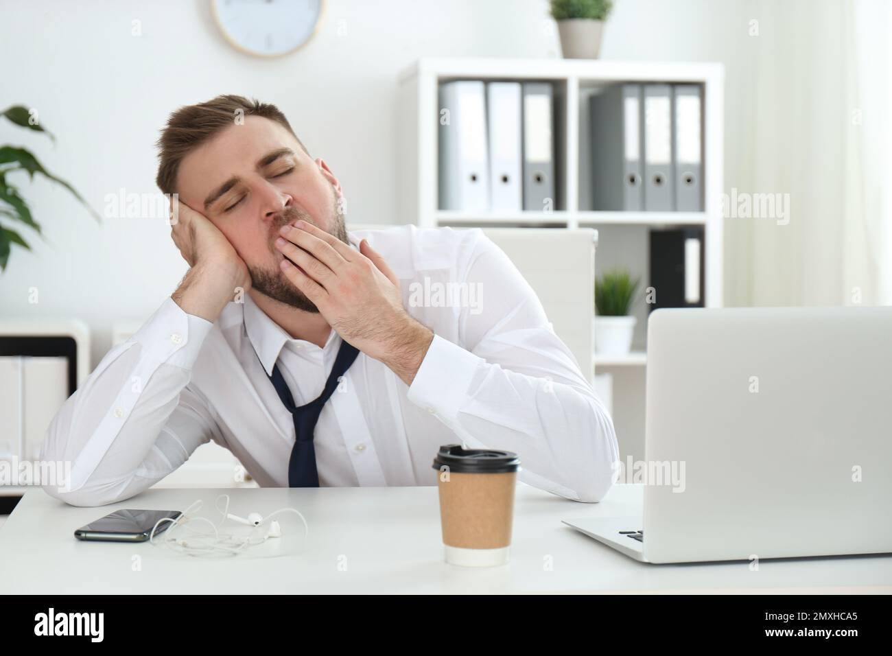 Lazy young man yawning at table in office Stock Photo - Alamy