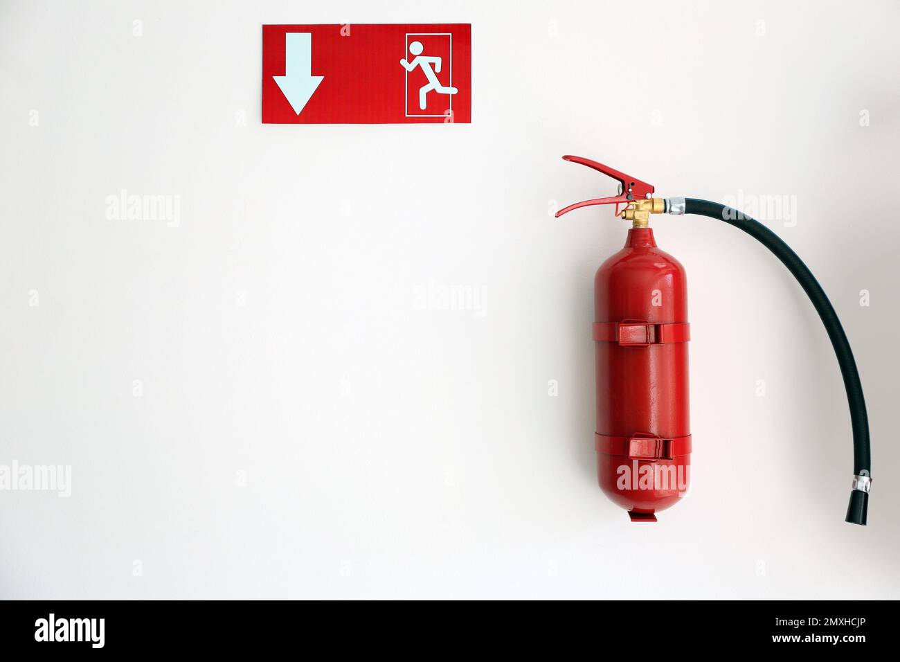 Fire extinguisher and emergency exit sign on white wall, space for text ...