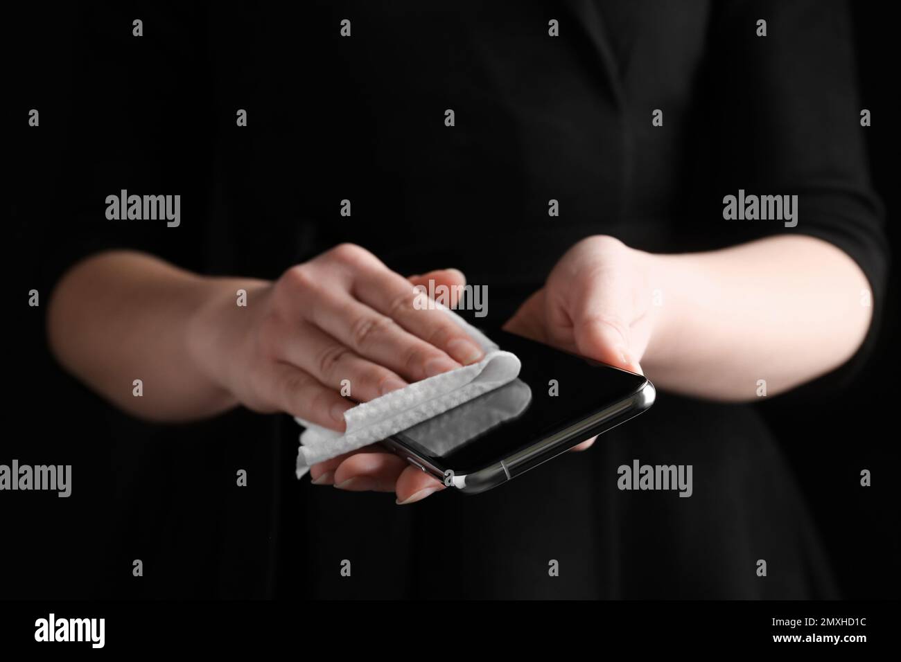 Woman cleaning mobile phone with antiseptic wipe on black background ...