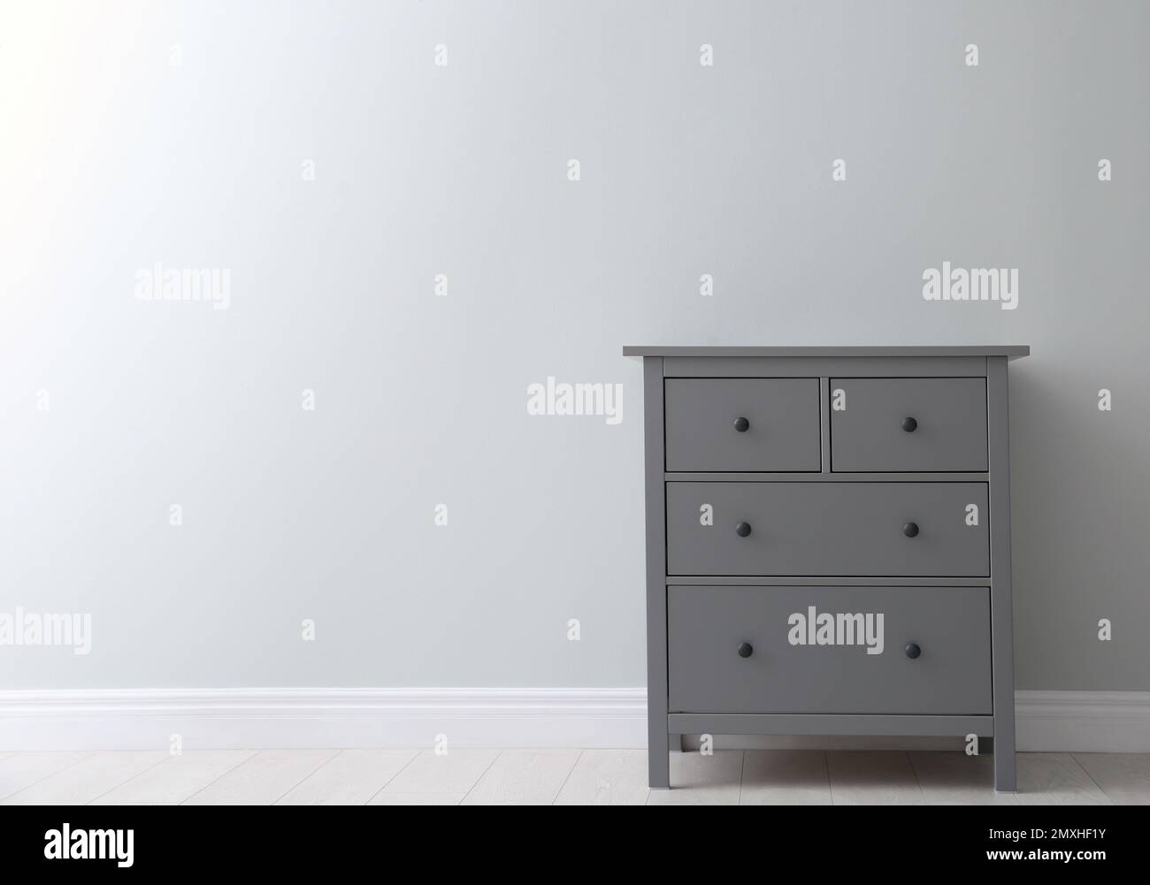 Modern grey chest of drawers near light wall in room, space for text ...