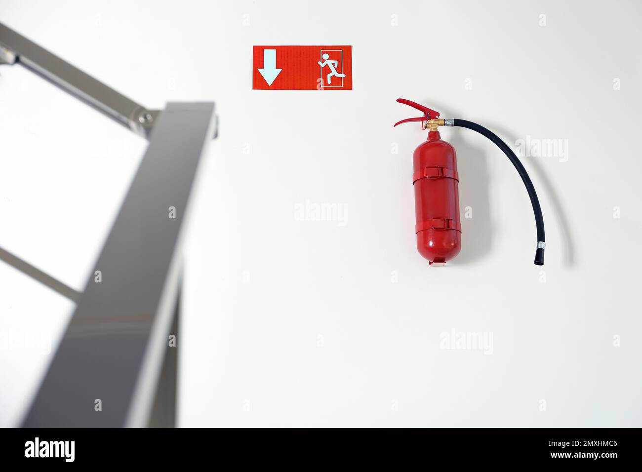 Fire extinguisher and emergency exit sign on white wall near staircase ...
