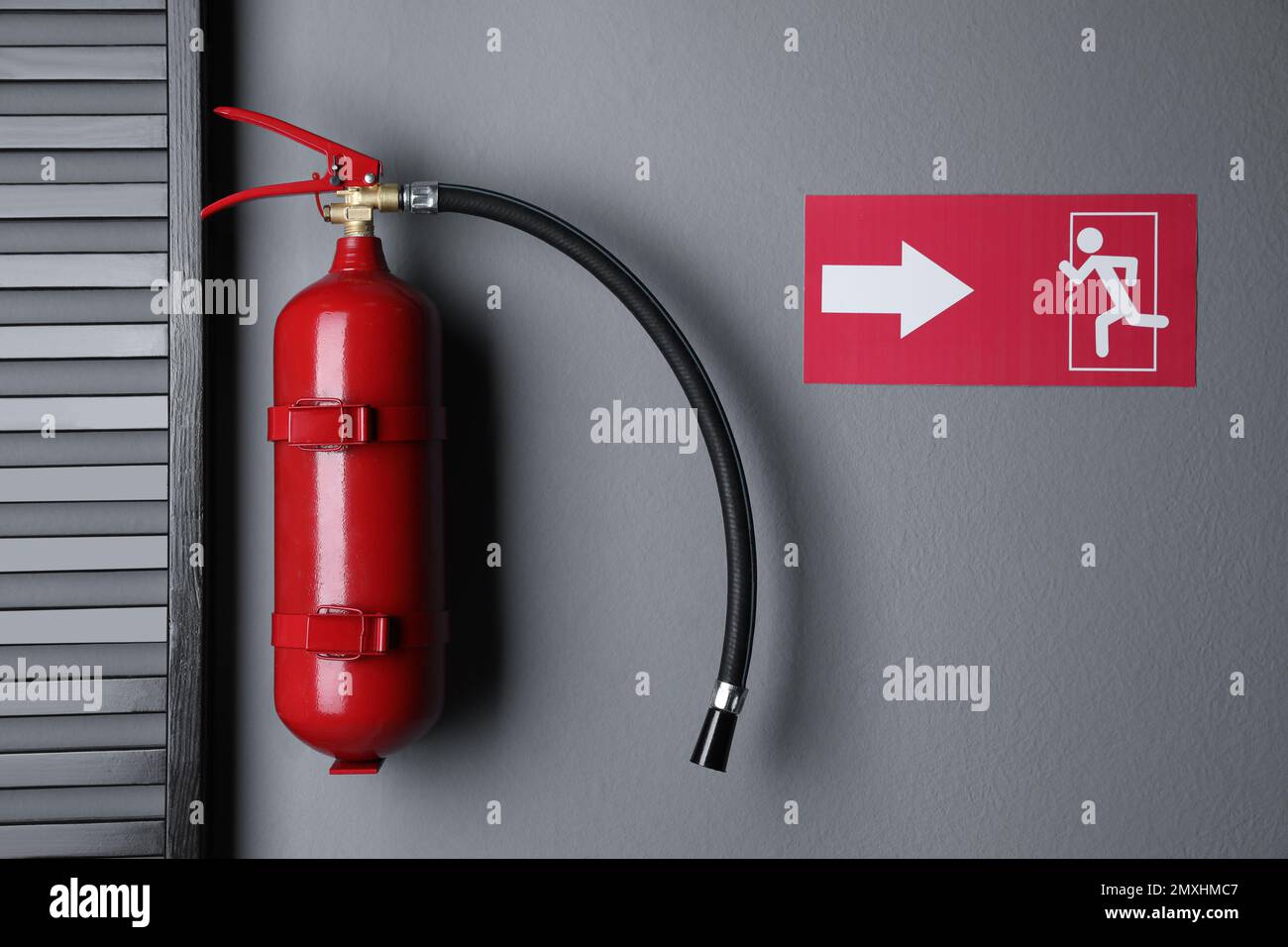 Fire extinguisher and emergency exit sign on grey wall indoors Stock ...