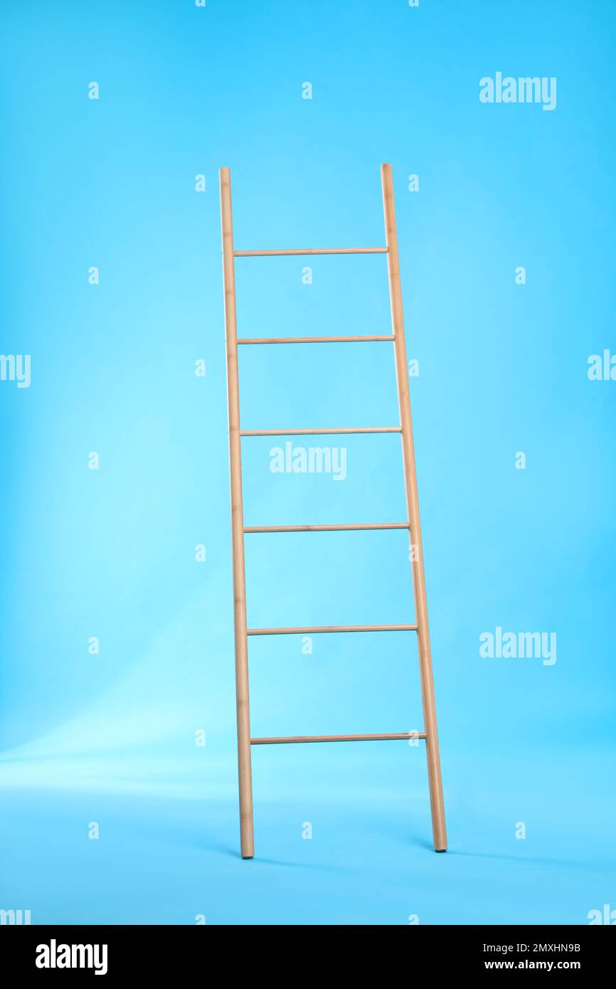 Modern wooden ladder on light blue background Stock Photo - Alamy