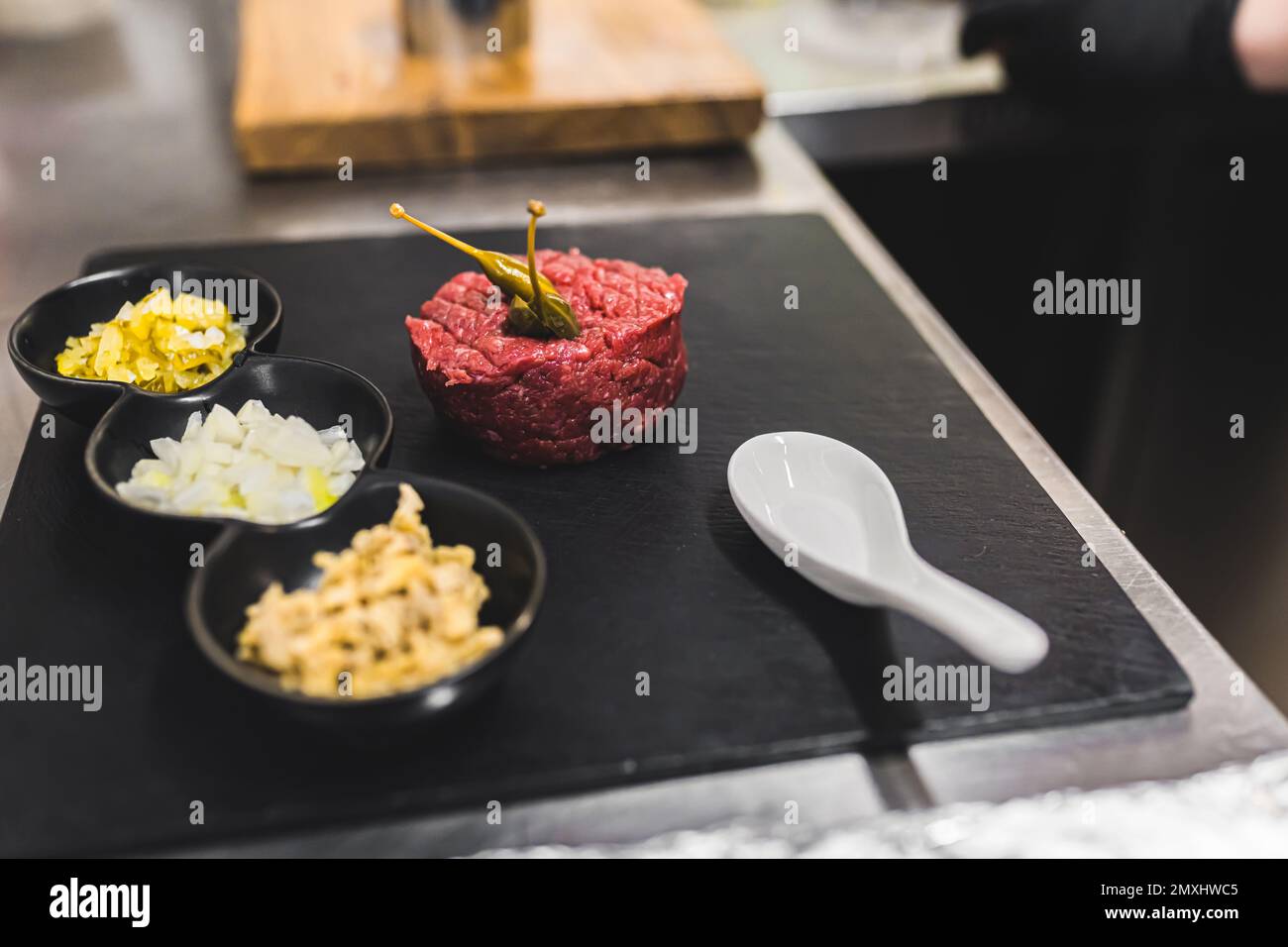 Plating smoked beef tartare on black wooden board with various ...