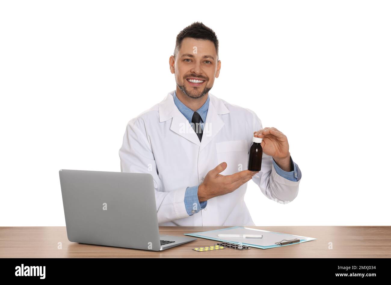 Professional pharmacist with syrup and laptop at table against white ...